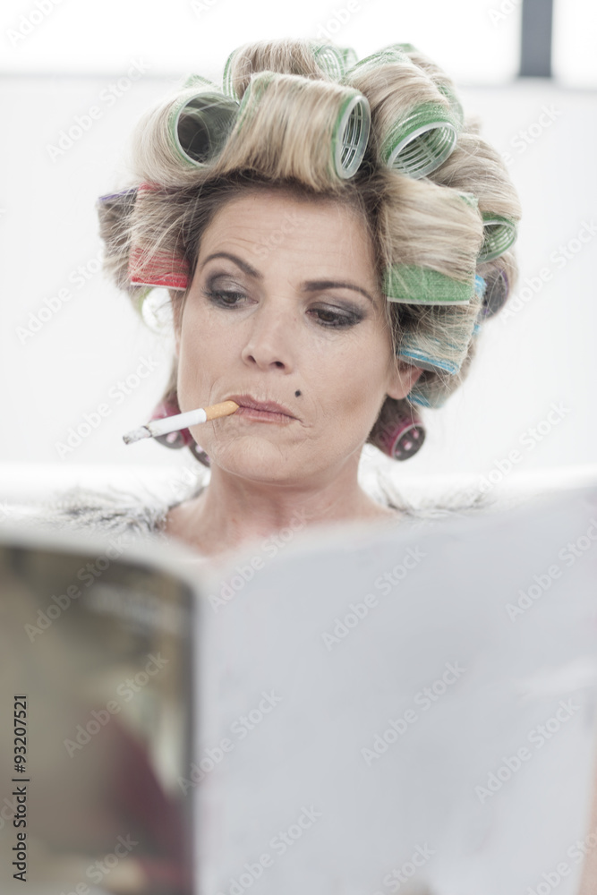 Portrait of woman with hair curlers and magazine smoking a cigarette ...