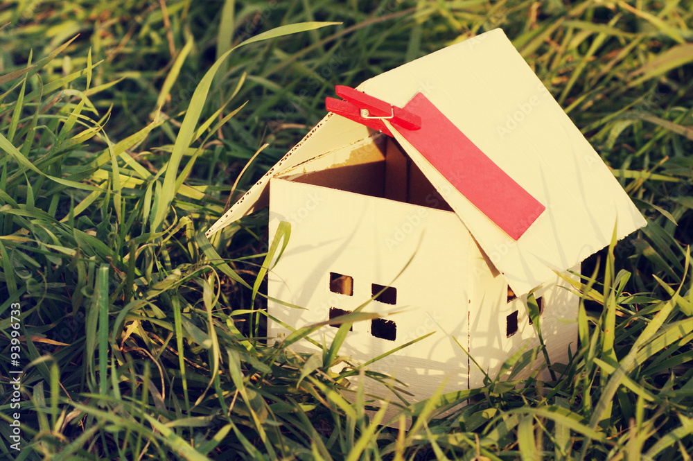 House from paper with an empty red card in a green grass. Model of ...