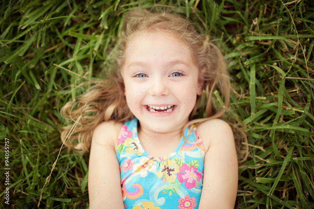 Top view portrait of a smiling shy little girl lying on green grass ...