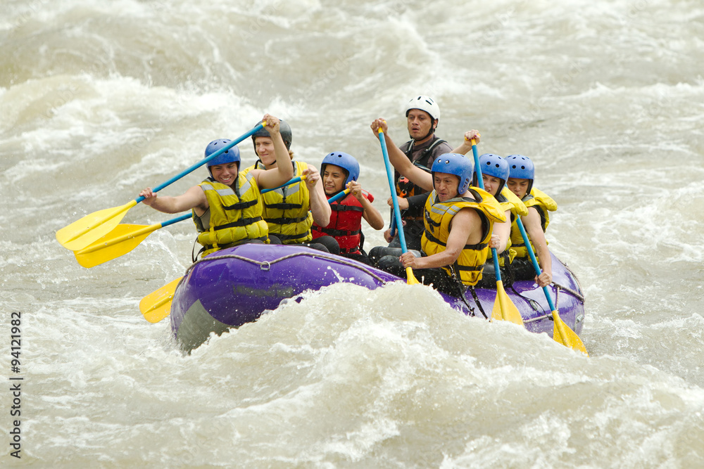 A group of energetic people in a white raft, navigating through green ...