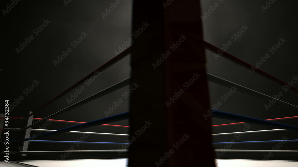 A pan across a empty regular boxing ring surrounded by ropes spotlit in ...