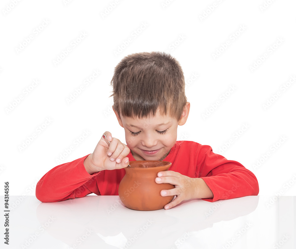 The sick five-year-old boy sits at a white table and eats with a spoon ...