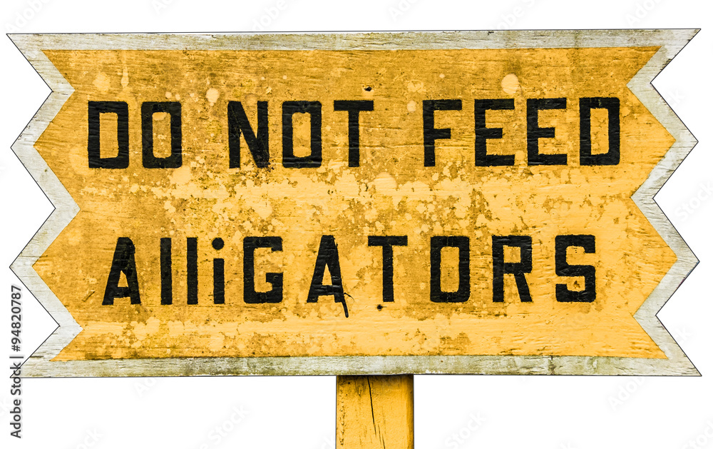 Yellow wooden warning sign with black text. Do not feed Alligators ...