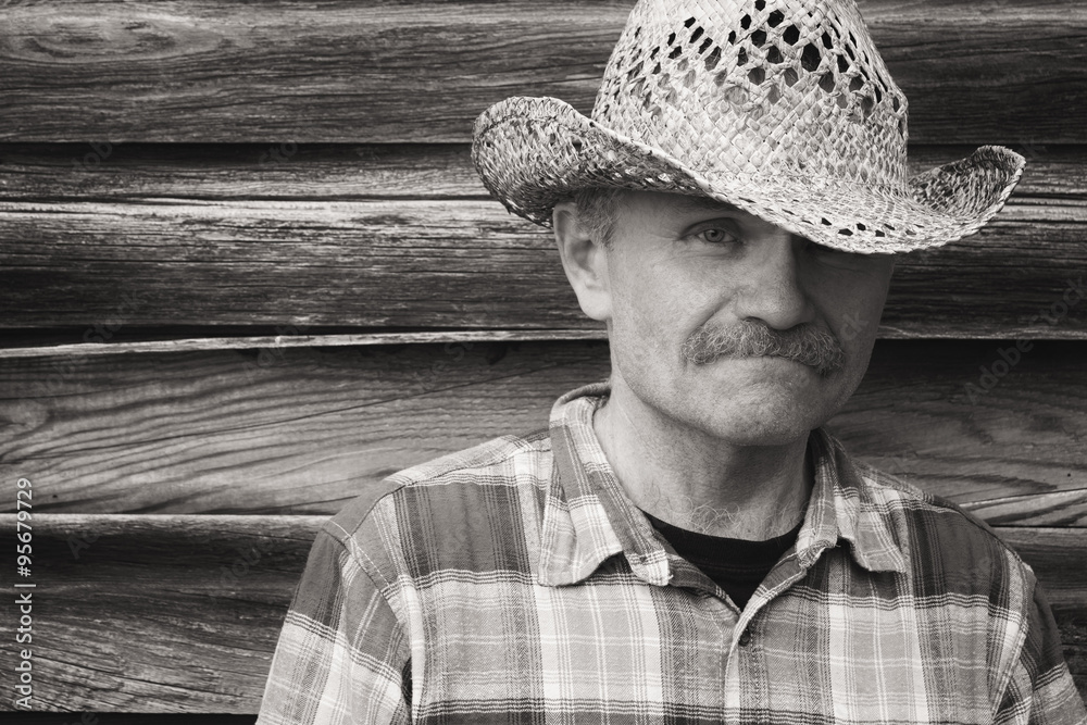 horizontal sepia head shot of a cowboy standing next to an old wood ...