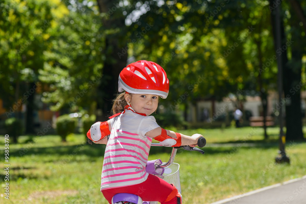 Beautiful little girl with colorful red safety helmet, riding a bicycle ...