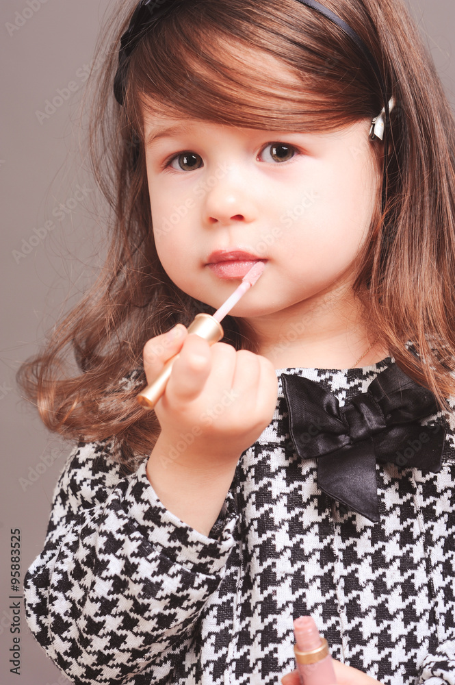 Kid girl applying lip gloss on lips in room. Looking at camera. Child ...