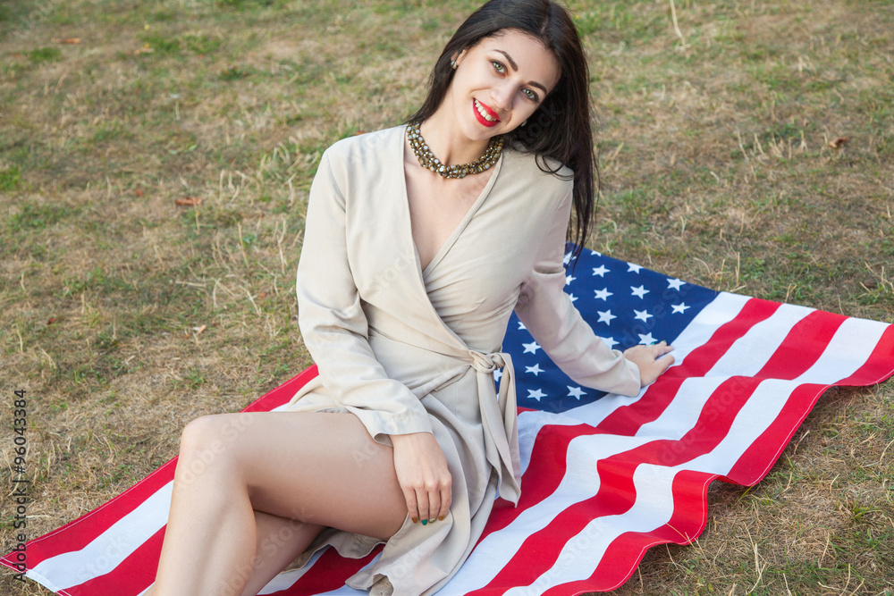 Beautiful sexy young woman with classic dress lying down on american flag in the park. fashion ...