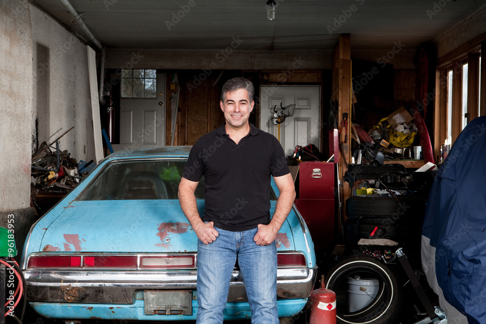 Man standing in his cluttered garage next to an old car. Stock Photo ...