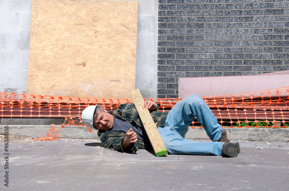 A fallen and injured construction worker in a hard hat laying on the ...