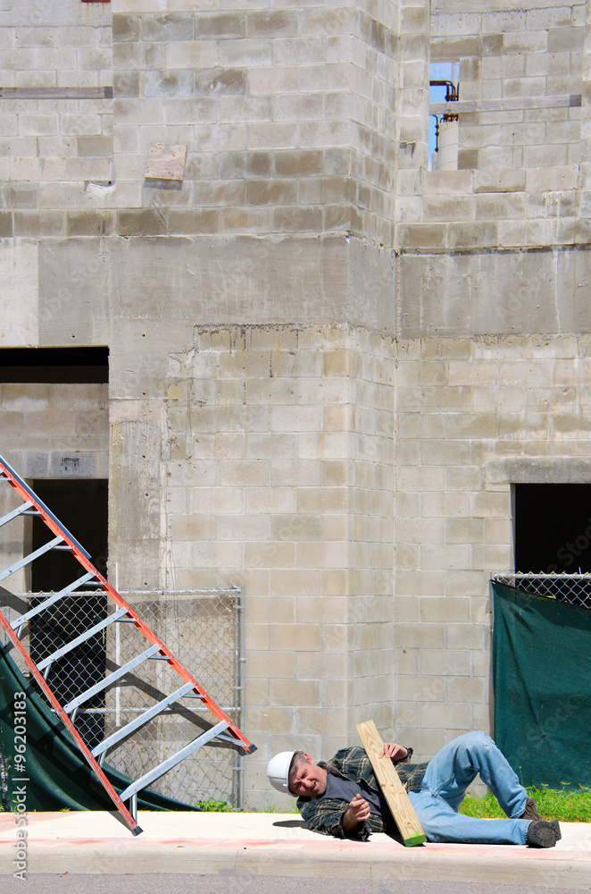 A fallen injured construction worker in a hard hat laying on the ground ...