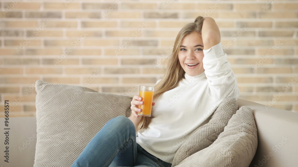 Cute girl sitting on sofa drinking juice looking at camera and smiling ...