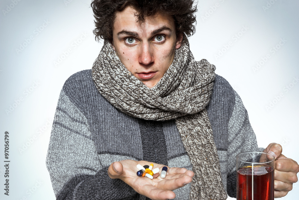 Ill man taking many pills. Young guy holding many pills and hot tea ...