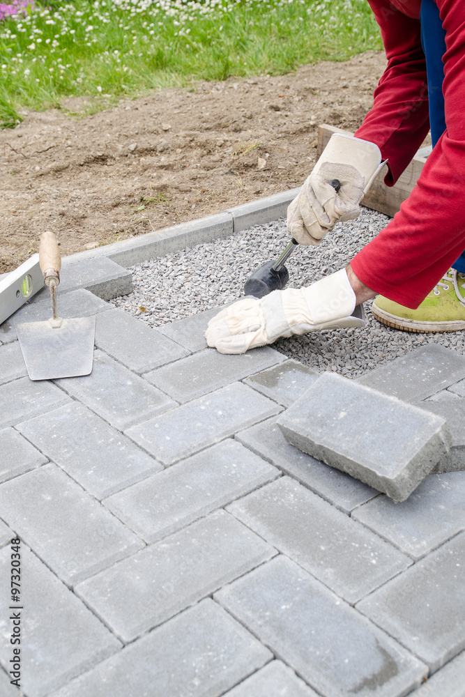 Bricklayer places concrete paving stone blocks for building up a patio ...