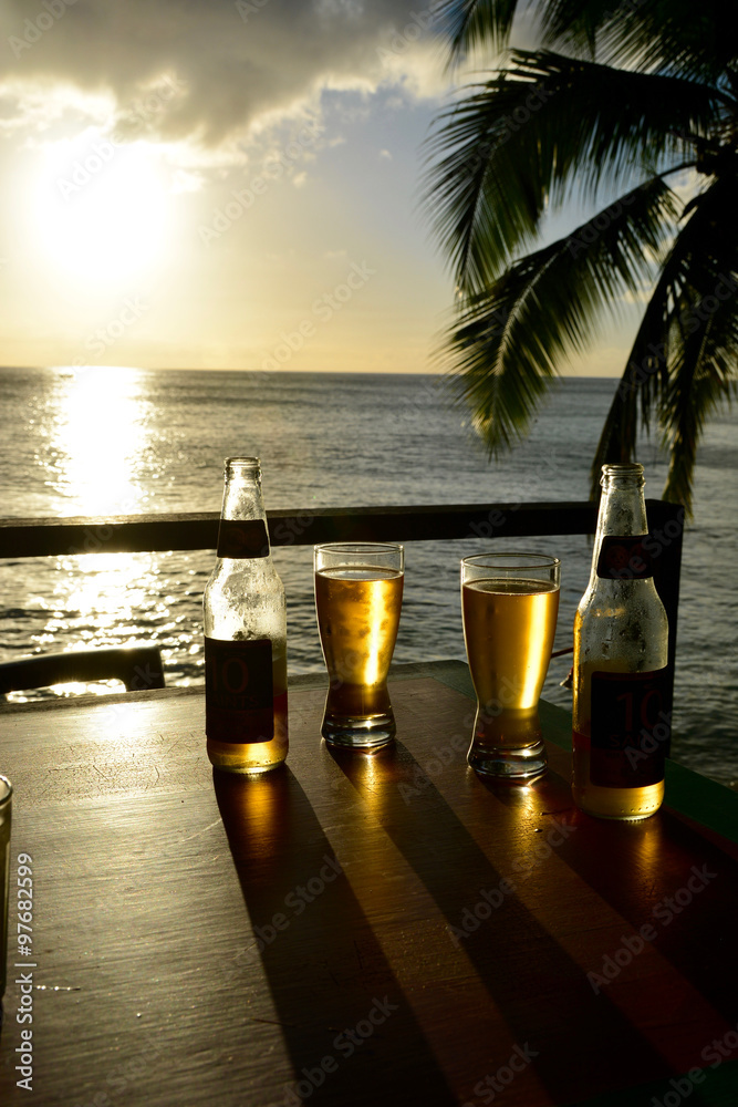 Two beers over sunset beach/ 2 bottles and glass of beer with Palm tree ...