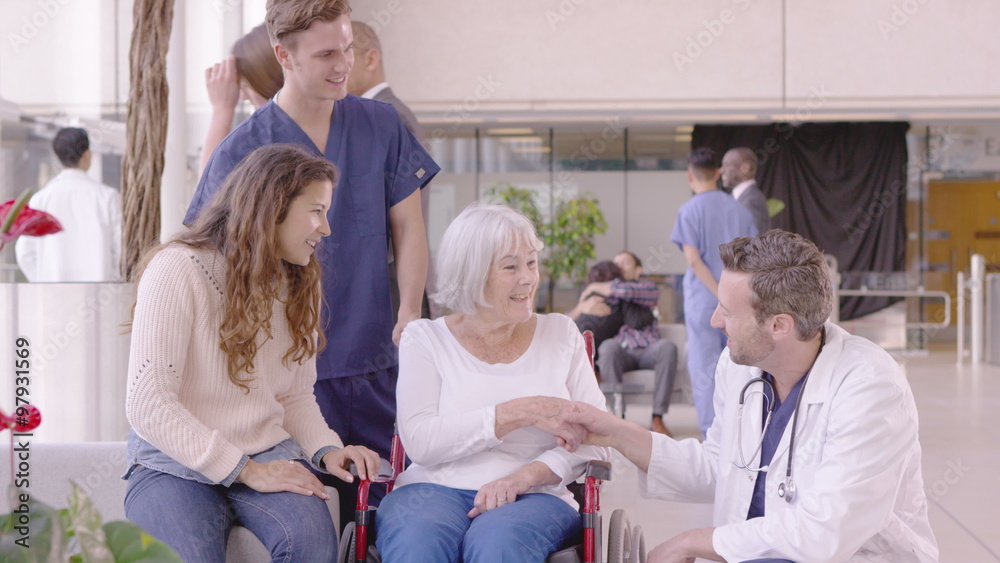 Caring medical staff talking to patient in wheelchair in busy modern ...