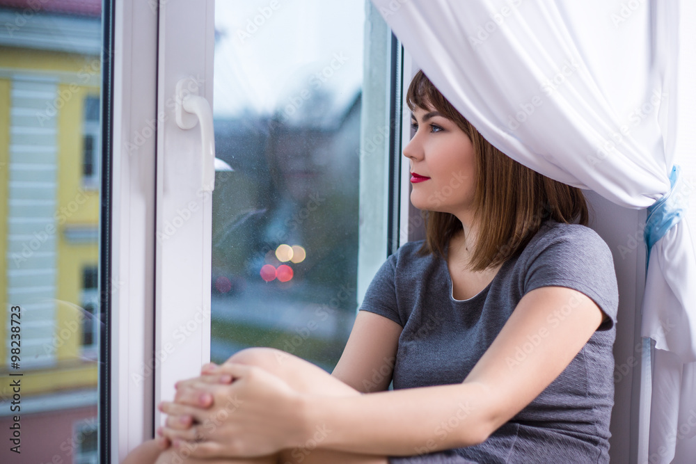 portrait of charming woman sitting on window sill and looking th Stock ...
