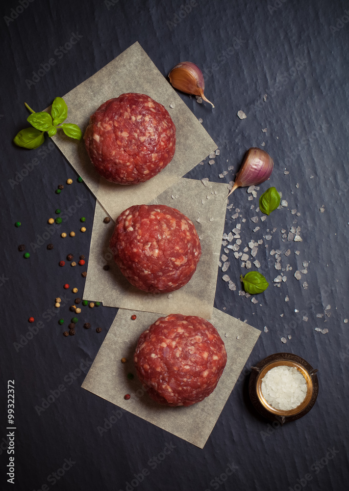 Poster Raw ground beef meat steak cutlets with herbs and spices on blac ...