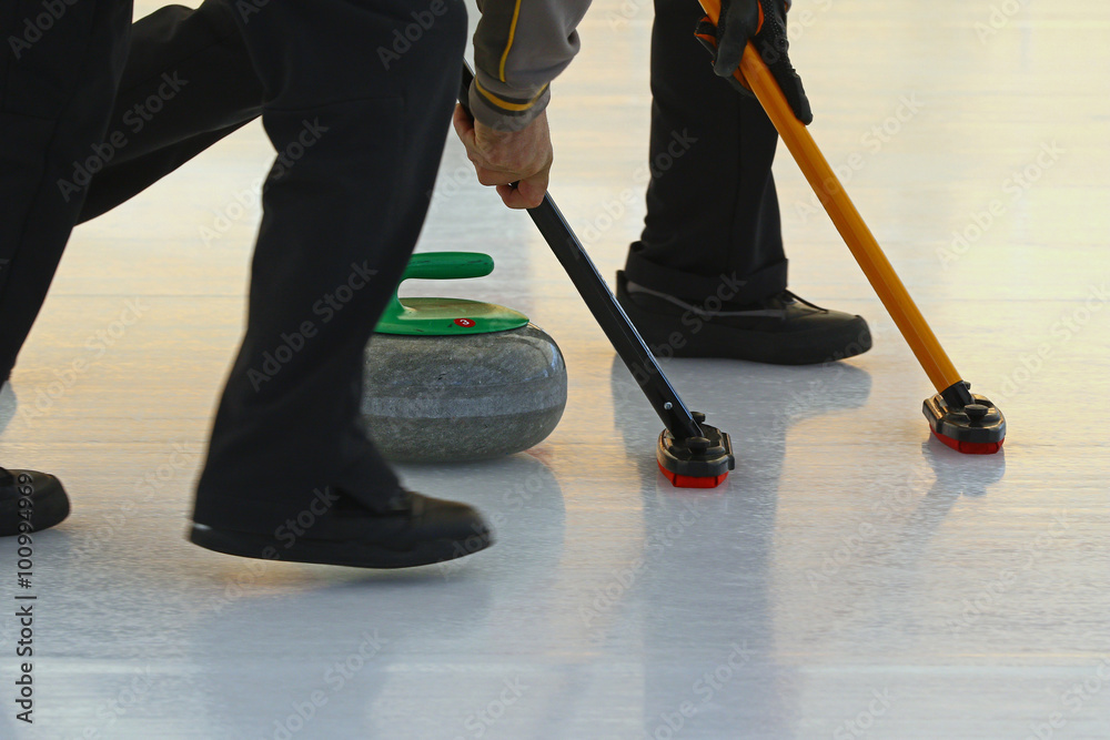 Curling stone sliding down the ice with player's feet running in front ...
