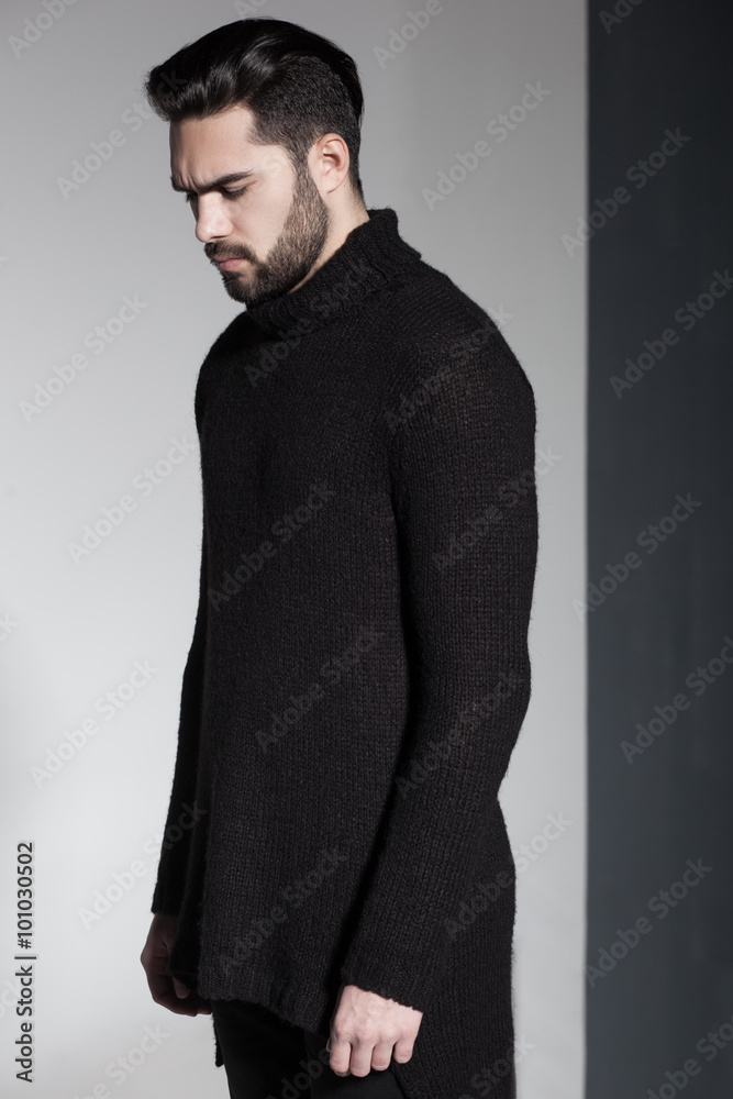 sexy fashion man model in black sweater, jeans and boots posing ...