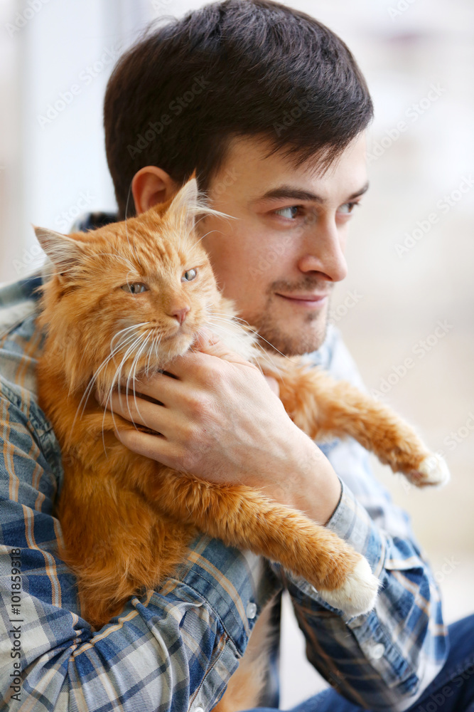 Young man with fluffy red cat looking out the window Stock Photo ...