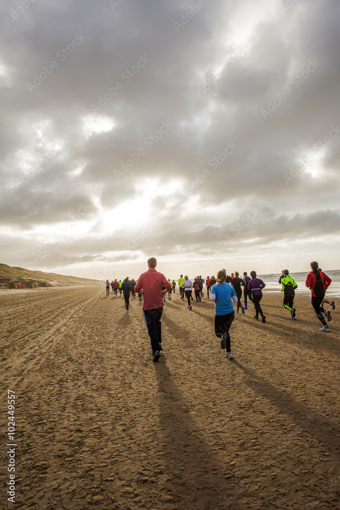 A group of back lit people in colorful outfits are running on a beach ...