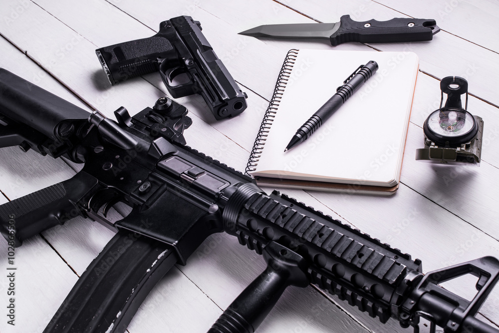 Notebook,pen,rifle,pistol,knife and compass on table.Top view/Open ...