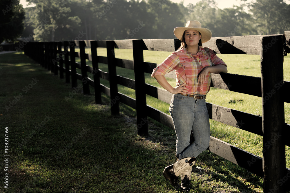 Cowgirl woman in cowboy hat flannel shirt and jeans leaning on country ...