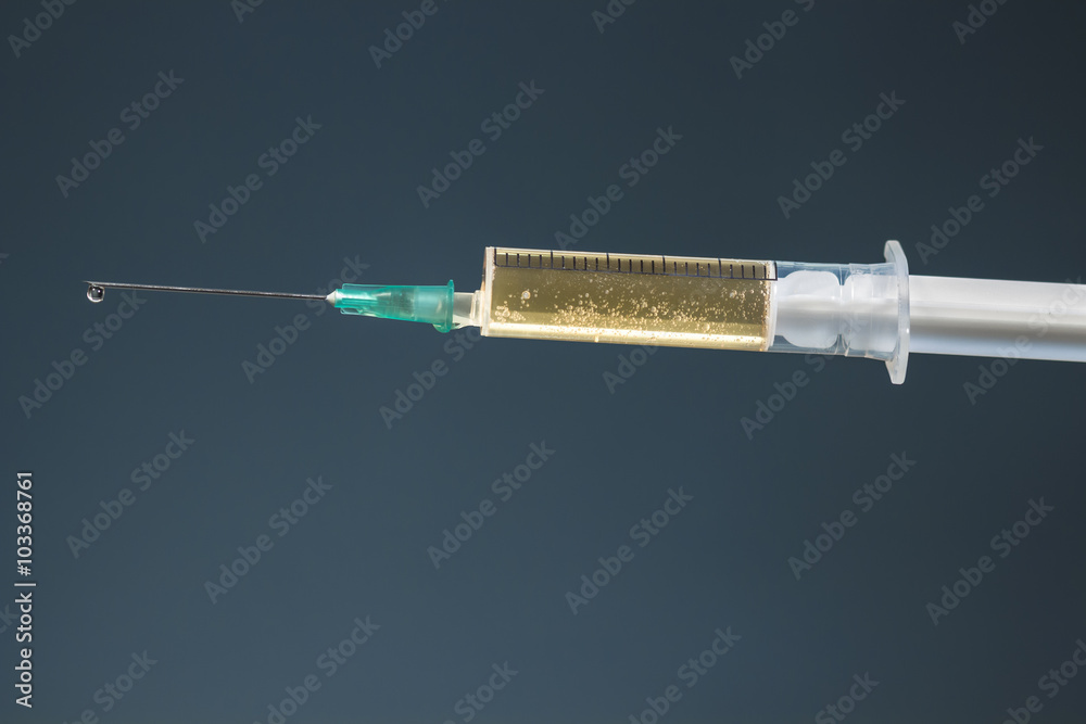 Hypodermic needle with drop at its tip and syringe with dark yellow ...