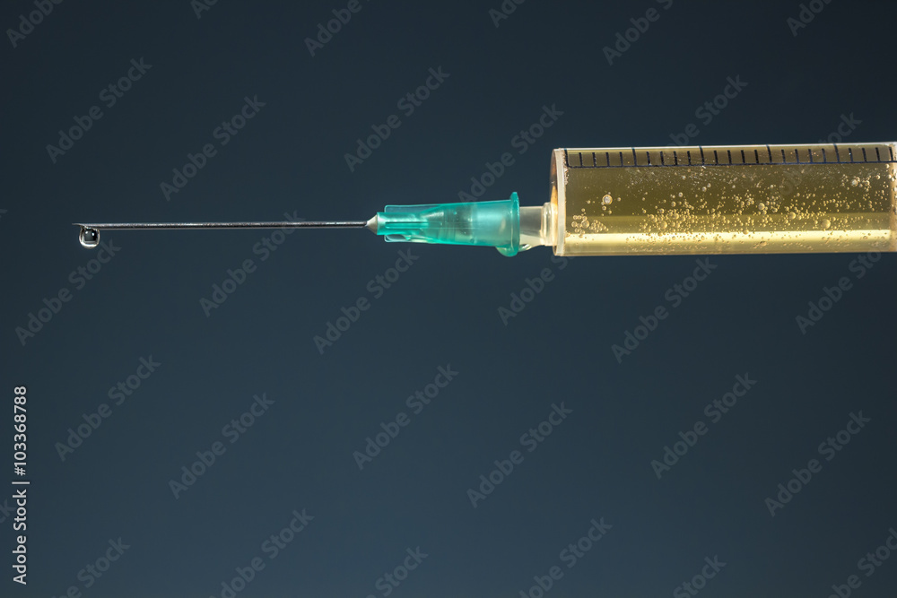 Hypodermic needle with a drop at its tip and syringe with dark yellow ...