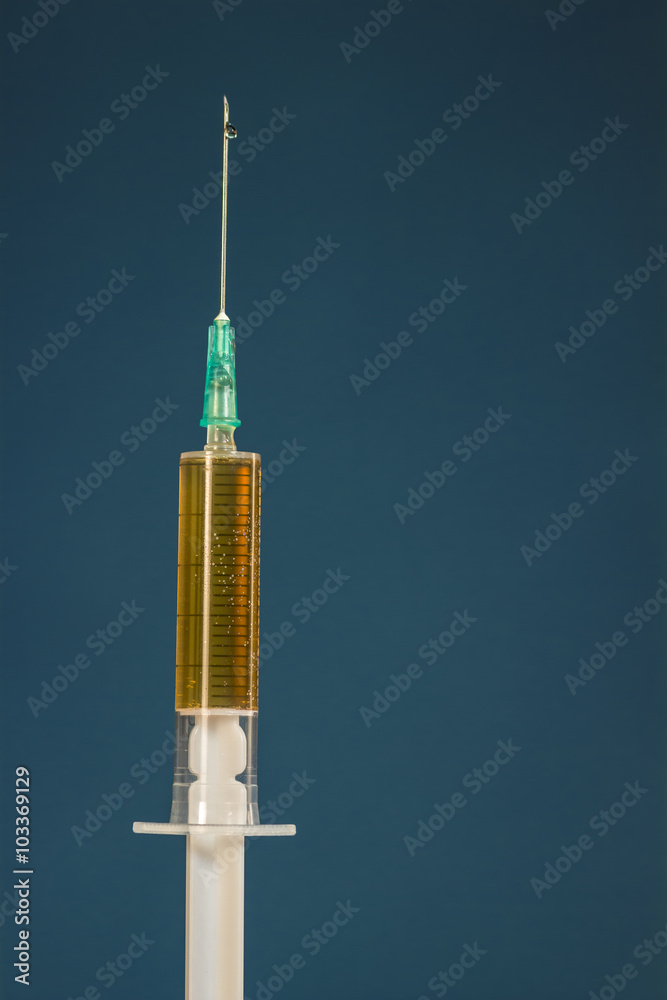 Hypodermic needle with a drop at its tip and syringe with dark yellow ...