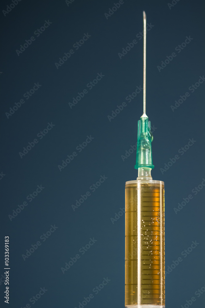 Hypodermic needle and syringe with dark yellow drug, on dark blue ...