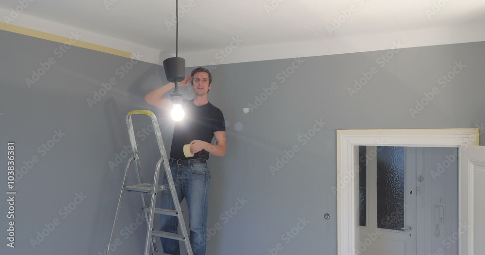 man standing on ladder and attaching ribbon tape on a wall. A light ...