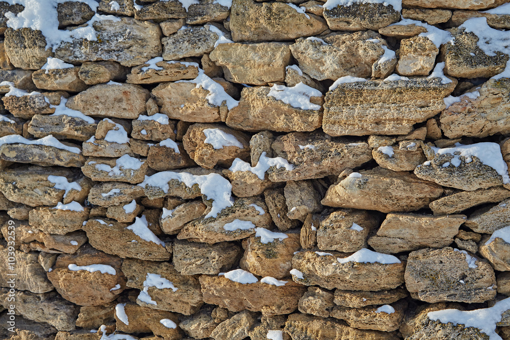 Grey-yellow stones in snow. A wall. Abstract. Structures. A background ...