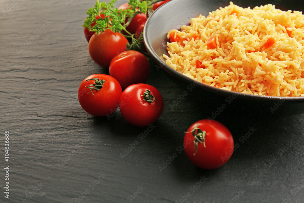 Stewed rice with a carrot and tomatoes on a plate over black background ...