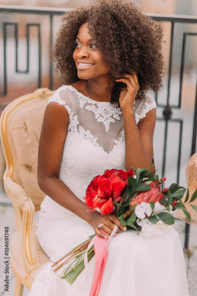 Charming african bride sitting on vintage terracotta chair and happily ...