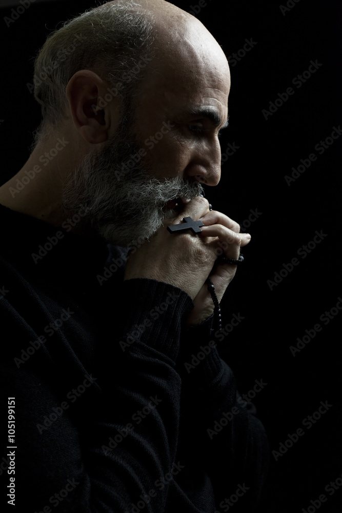 Intense shot of an old man, praying God with a rosary in his wrinkled ...