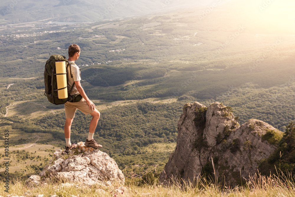 Backpacker on a high rock and looking at the big green valley ...