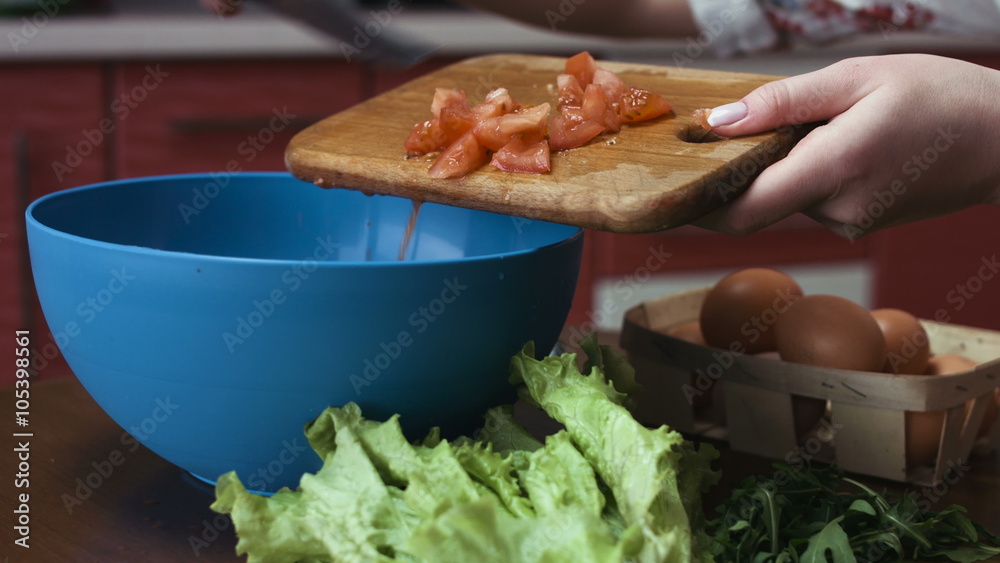 Tracking footage of female hands rake up tomato slices into a big blue ...