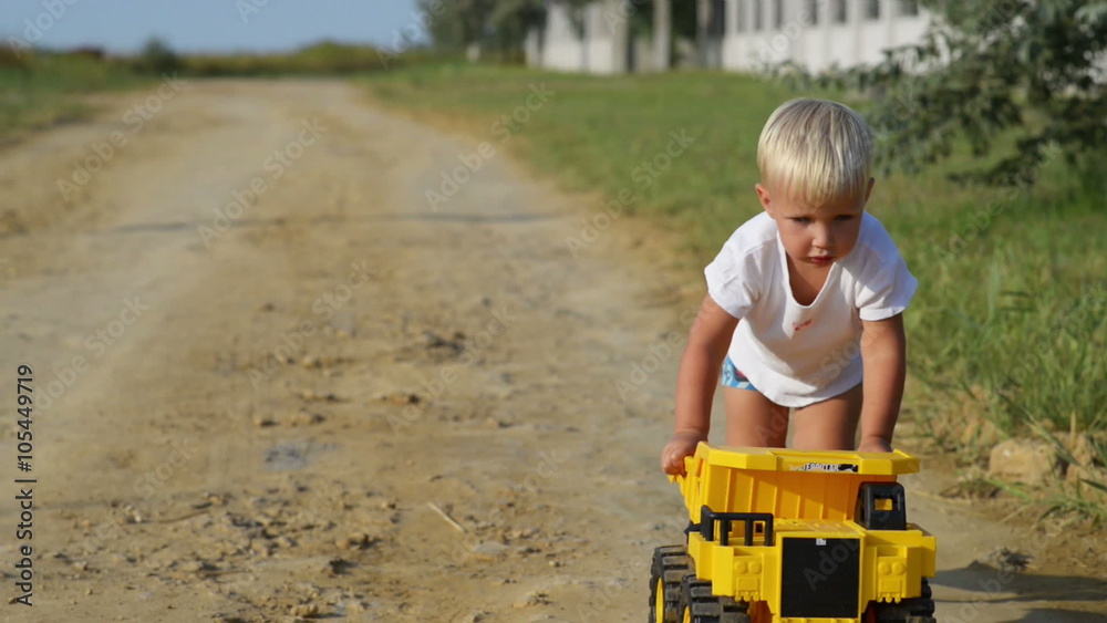 Little boy runs with big yellow car on the village roud. Slow motion ...