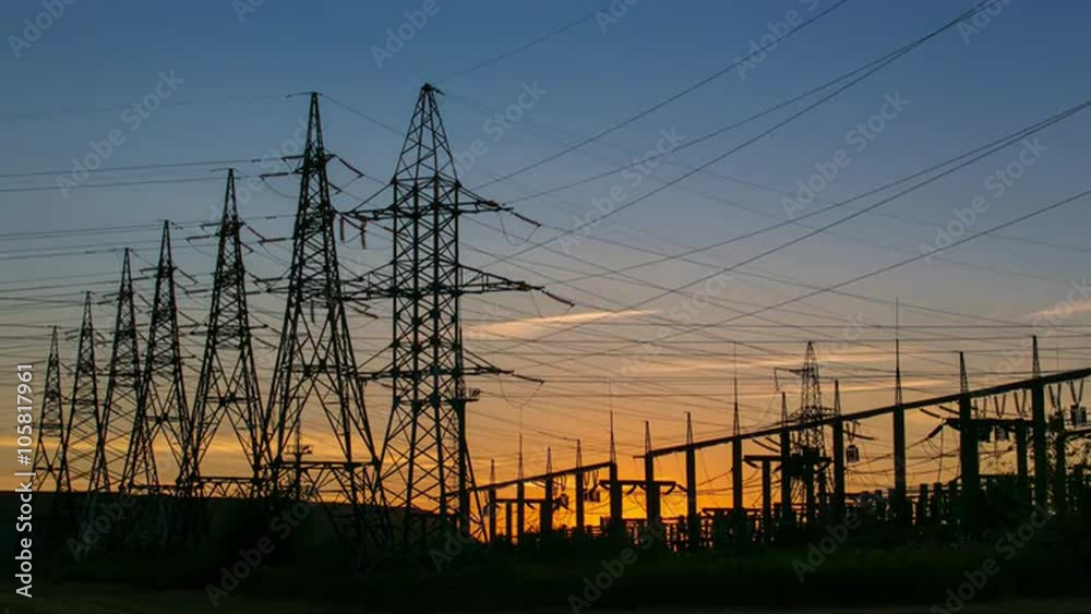 Time-lapse of sunset on a power plant. Sun going through electric high ...