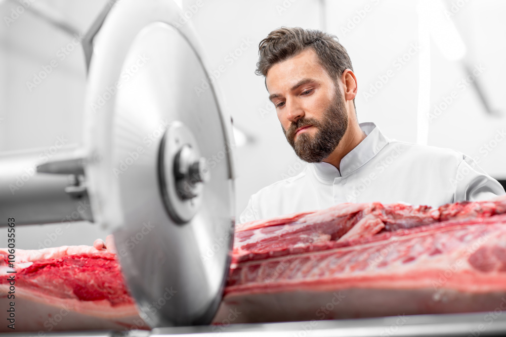 Handsome butcher cutting pork carcasse with big electric saw at the ...