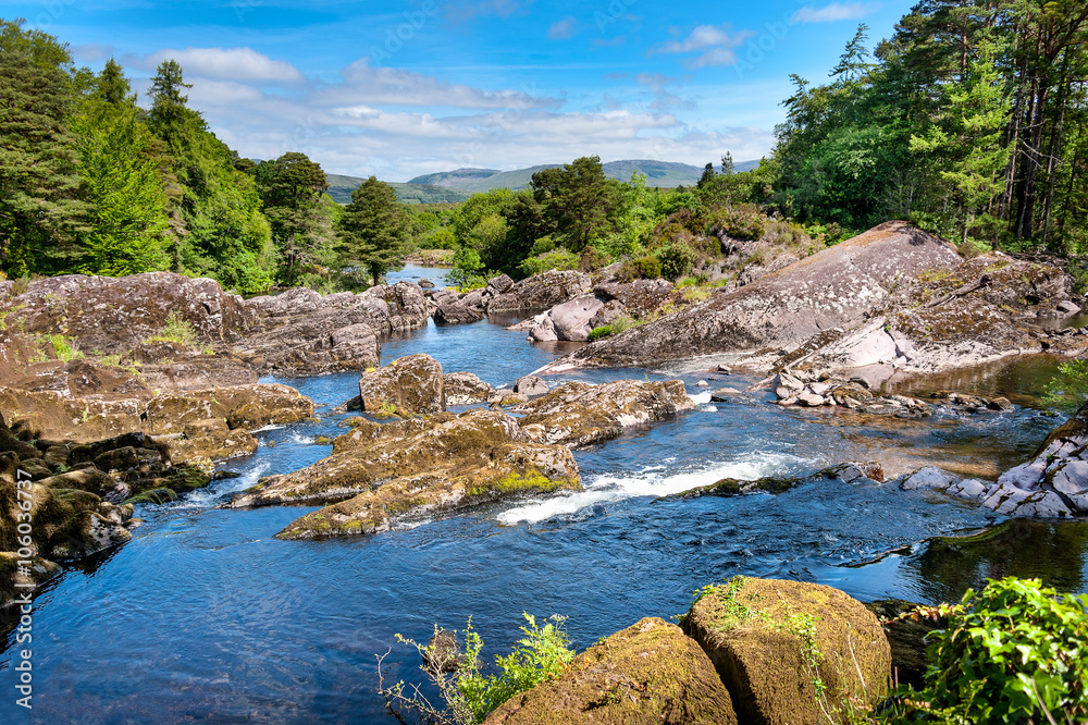 Scenic landscape with blue water which streams through rocky rapids ...