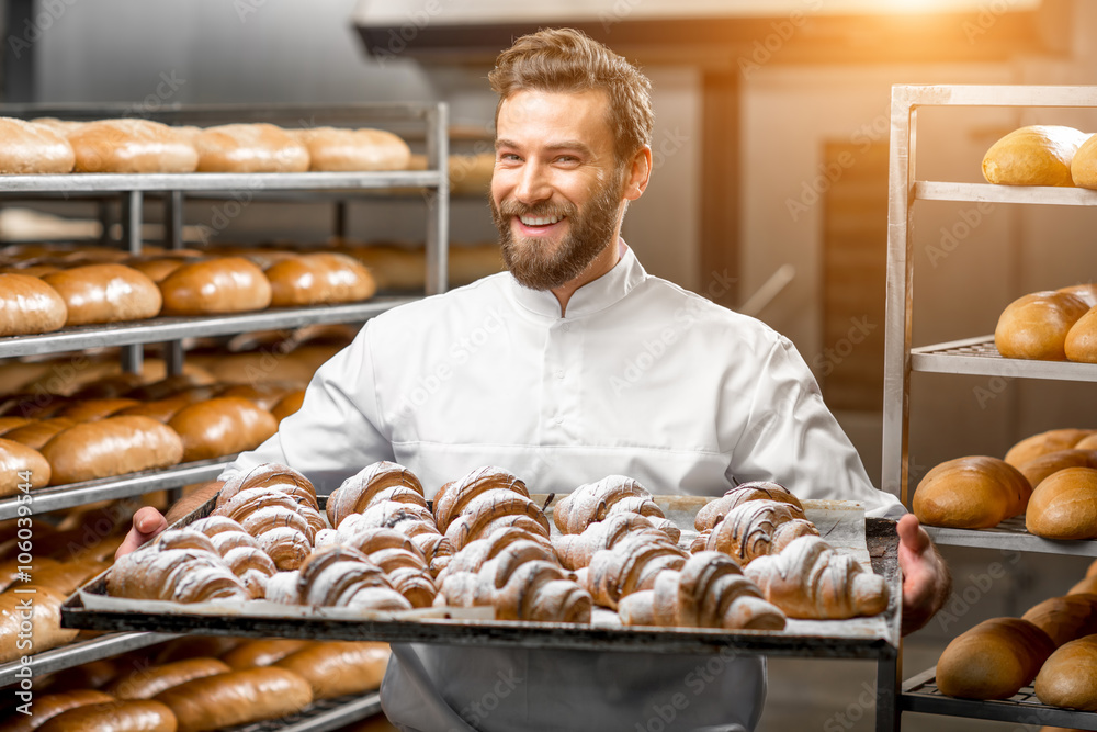 Handsome baker in uniform holding tray full of freshly baked croissants ...