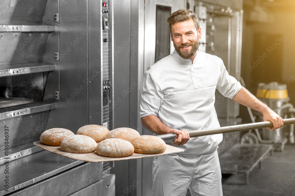 Handsome baker in uniform taking out with shovel freshly baked buckweat ...