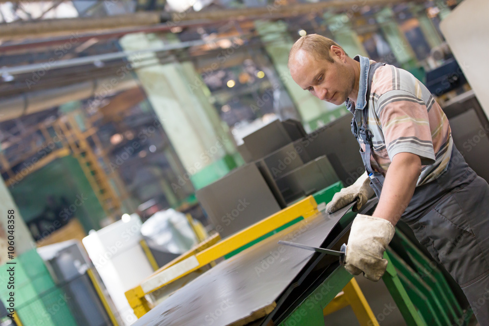 Factory man worker removing metal burrs from metal parts' surface with ...