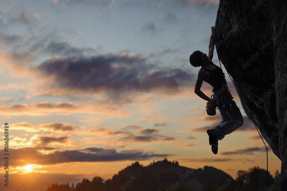 Silhouette of athletic female rock climber climbing steep rock wall ...