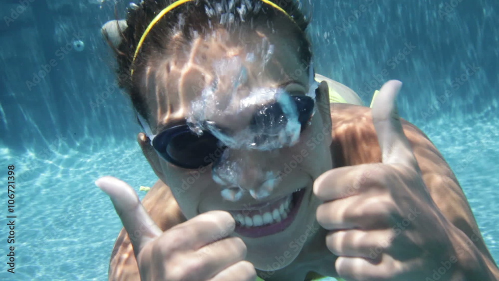 Woman swimming underwater in pool smiling happy giving thumbs up sign ...