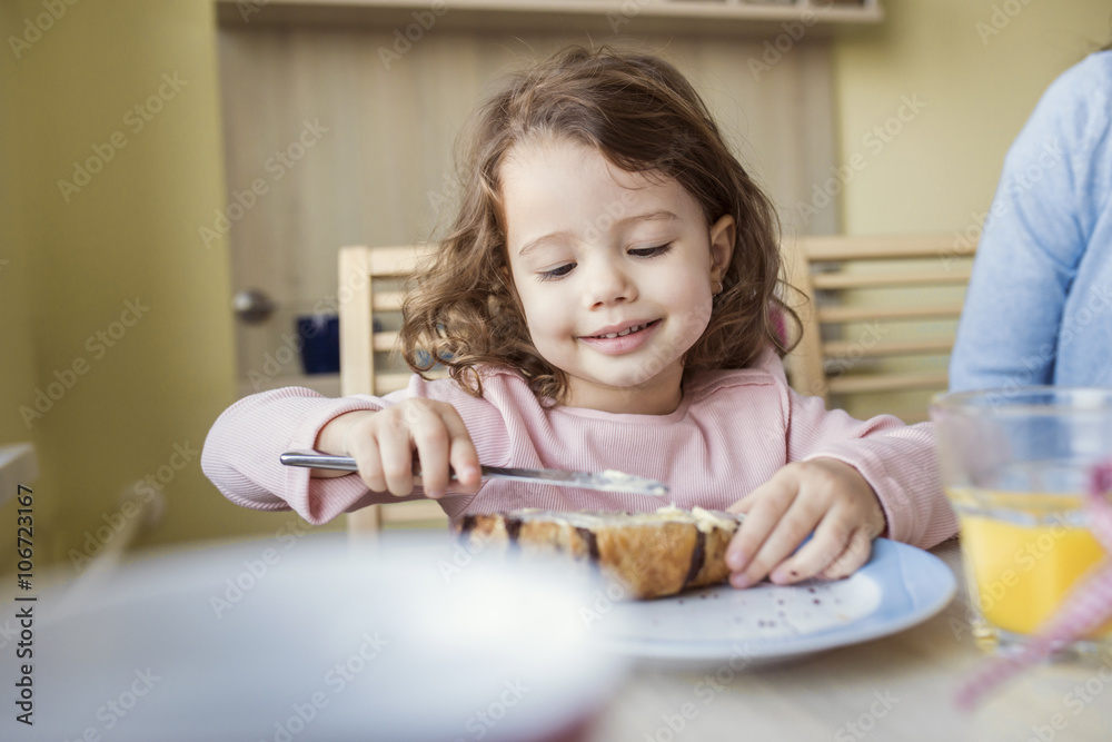 Portrait of smiling little girl spreading butter on her croissant Stock ...