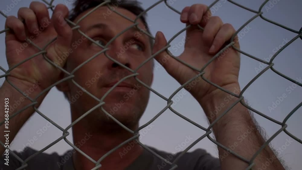 Closeup dusk shot of a male person looking through a fence with his ...