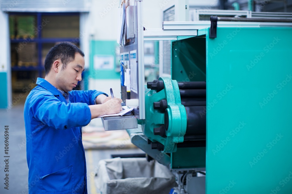 Worker at small parts manufacturing factory in China, writing paperwork ...